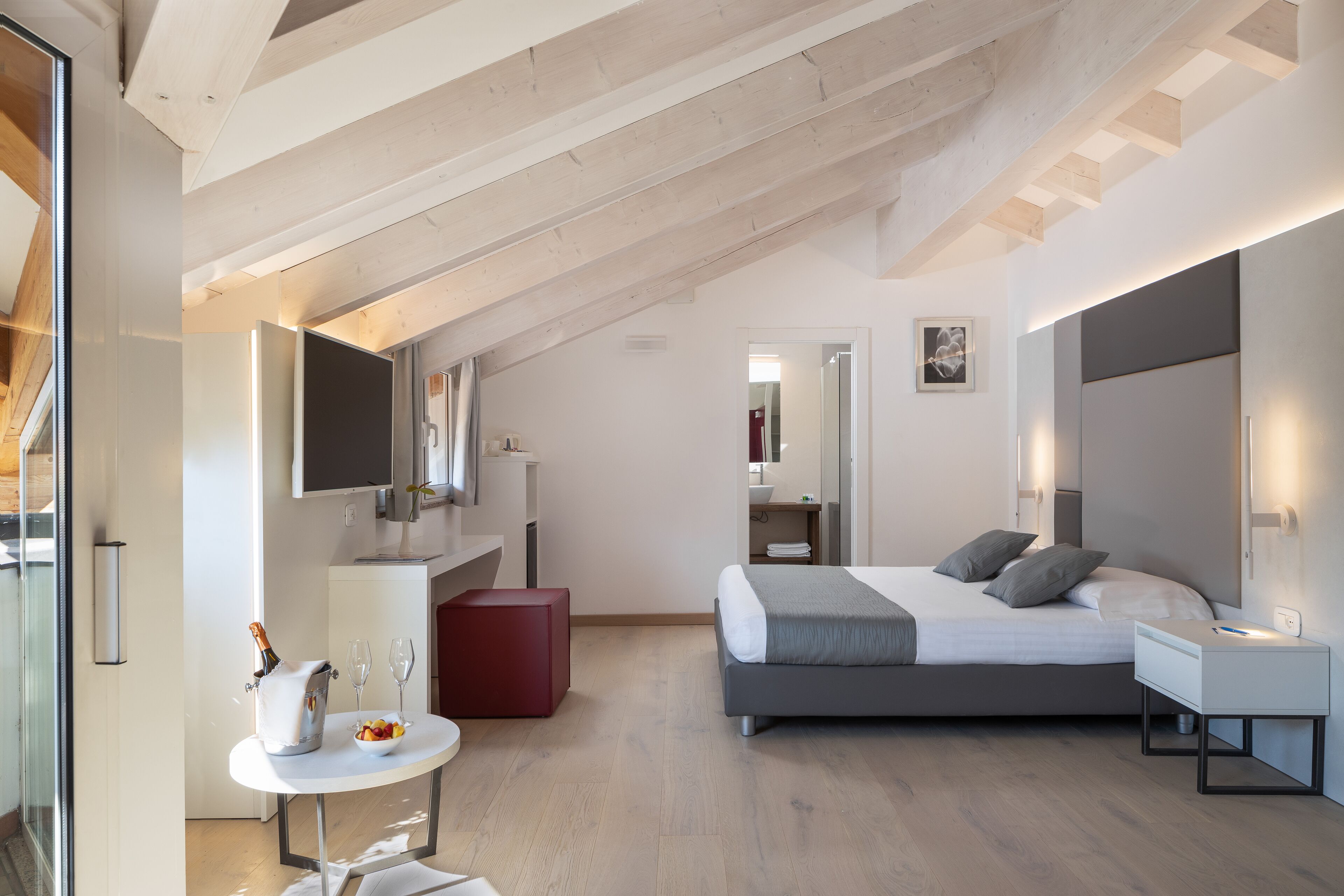 Quarto moderno com cama, mesa de cabeceira e uma pequena mesa com uma garrafa e copos.