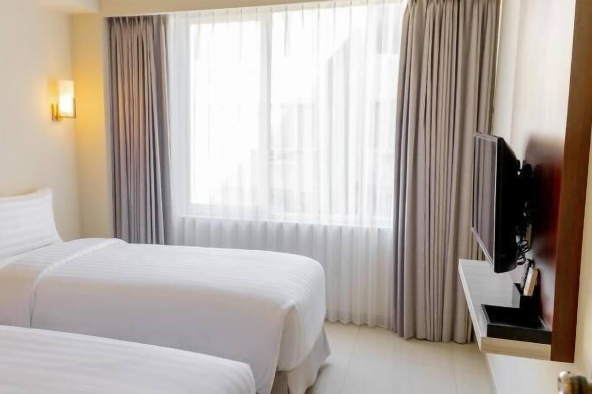 Quarto de hotel com duas camas, televisão e janela com cortinas.