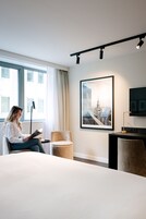 Quarto de hotel com uma cama grande, uma escrivaninha, uma cadeira, uma televisão e uma janela com cortinas.