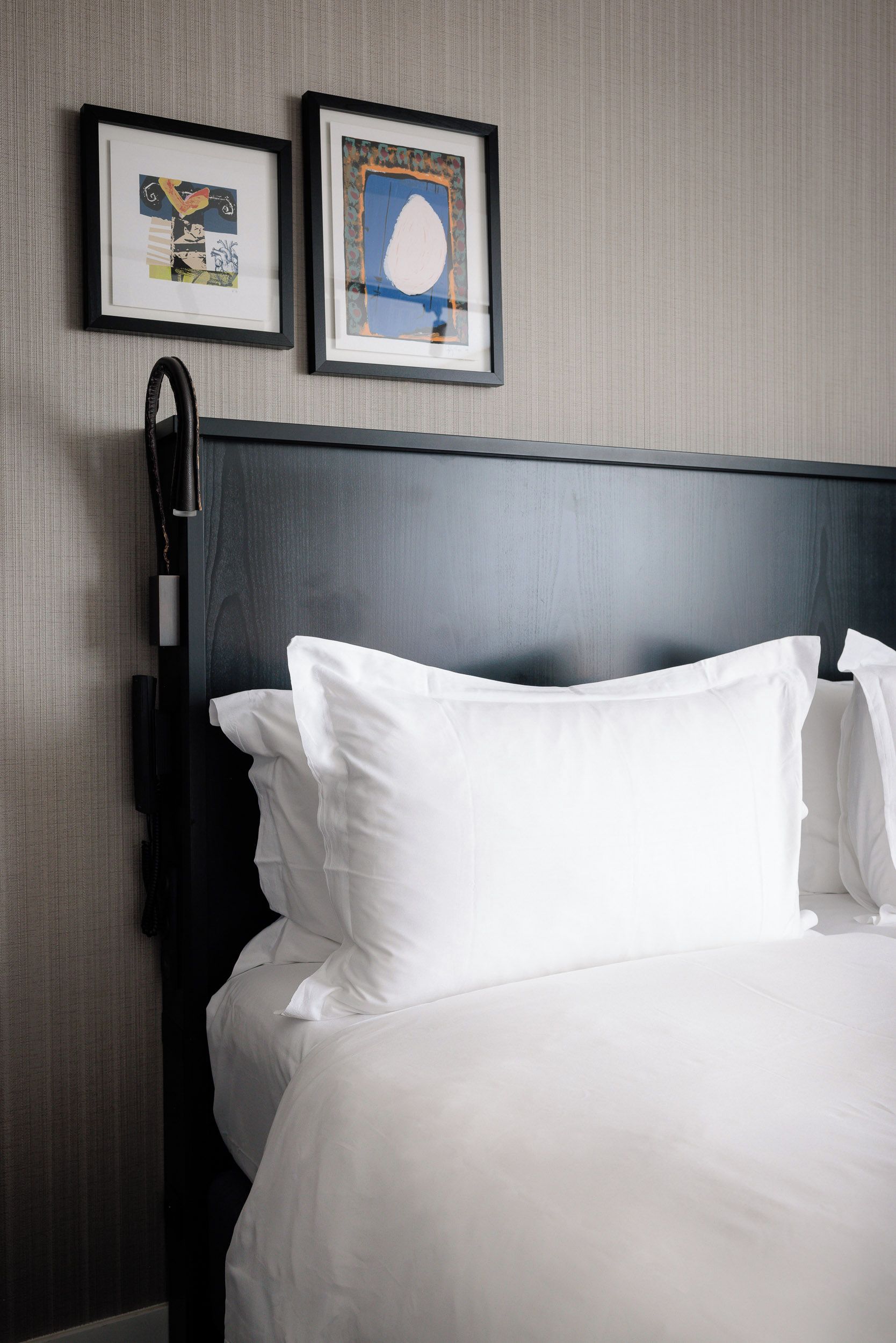 Quarto de hotel com uma cama, cabeceira e duas imagens emolduradas na parede.