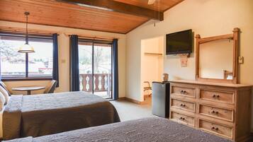 Quarto de hotel com duas camas, cômoda de madeira, televisão e varanda com mesa e cadeiras.