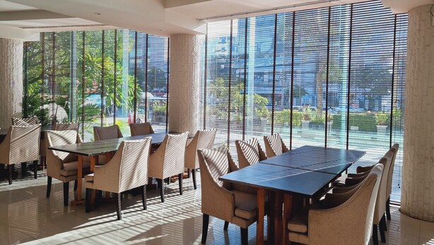 Uma sala de jantar moderna com uma mesa comprida e cadeiras, janelas amplas com persianas e um lustre.