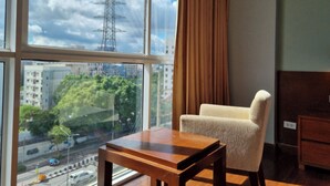 Quarto com uma janela grande, uma mesa de madeira, uma cadeira branca e um aparador de madeira.