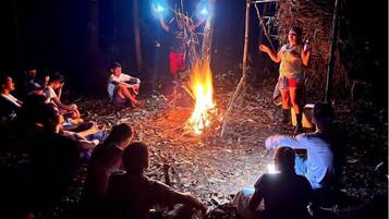 Um grupo de pessoas sentadas ao redor de uma fogueira em uma área arborizada.