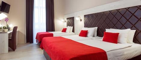 Quarto de hotel com três camas, uma escrivaninha com cadeira, televisão e janela com cortinas.