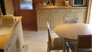 Interior em madeira com cozinha, incluindo micro-ondas, pia e mesa de jantar com cadeiras.