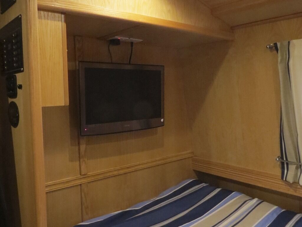Quarto de madeira com uma cama, uma televisão na parede e uma barra de cortina.