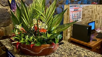 Uma mesa de recepção com uma planta em vaso, um calendário, um computador e um menu.