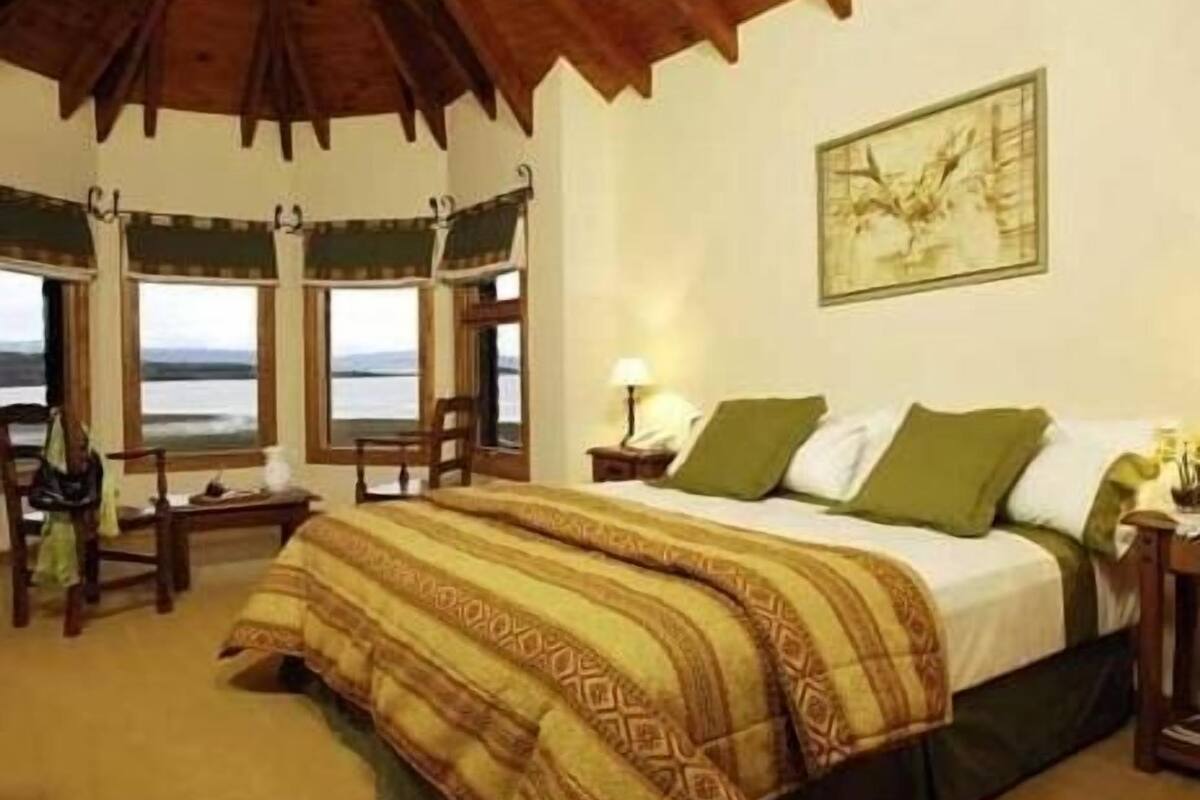 Quarto com cama, cadeira, mesa de cabeceira, abajur e janela com vista.