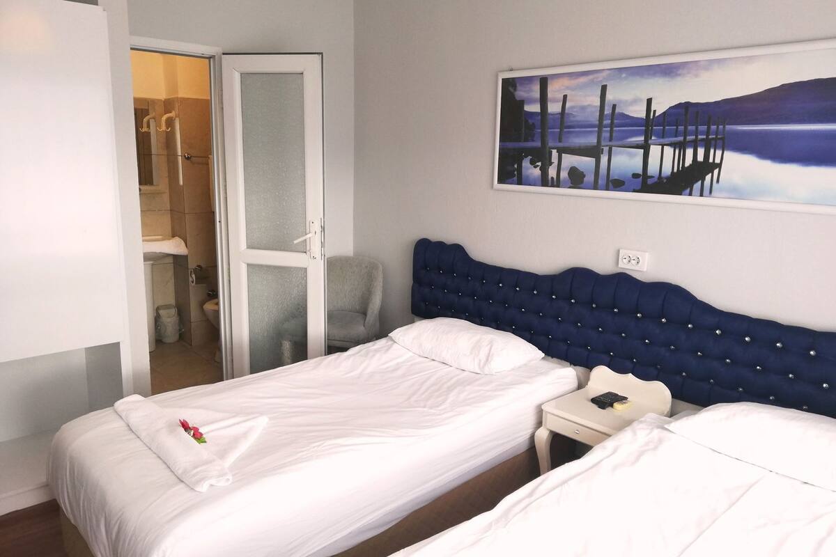 Quarto de hotel com duas camas, um banheiro e uma pintura de um cais.