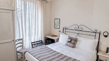 Quarto com cama, escrivaninha, cadeira, guarda-roupa, ventoinha no teto e janela com cortinas.