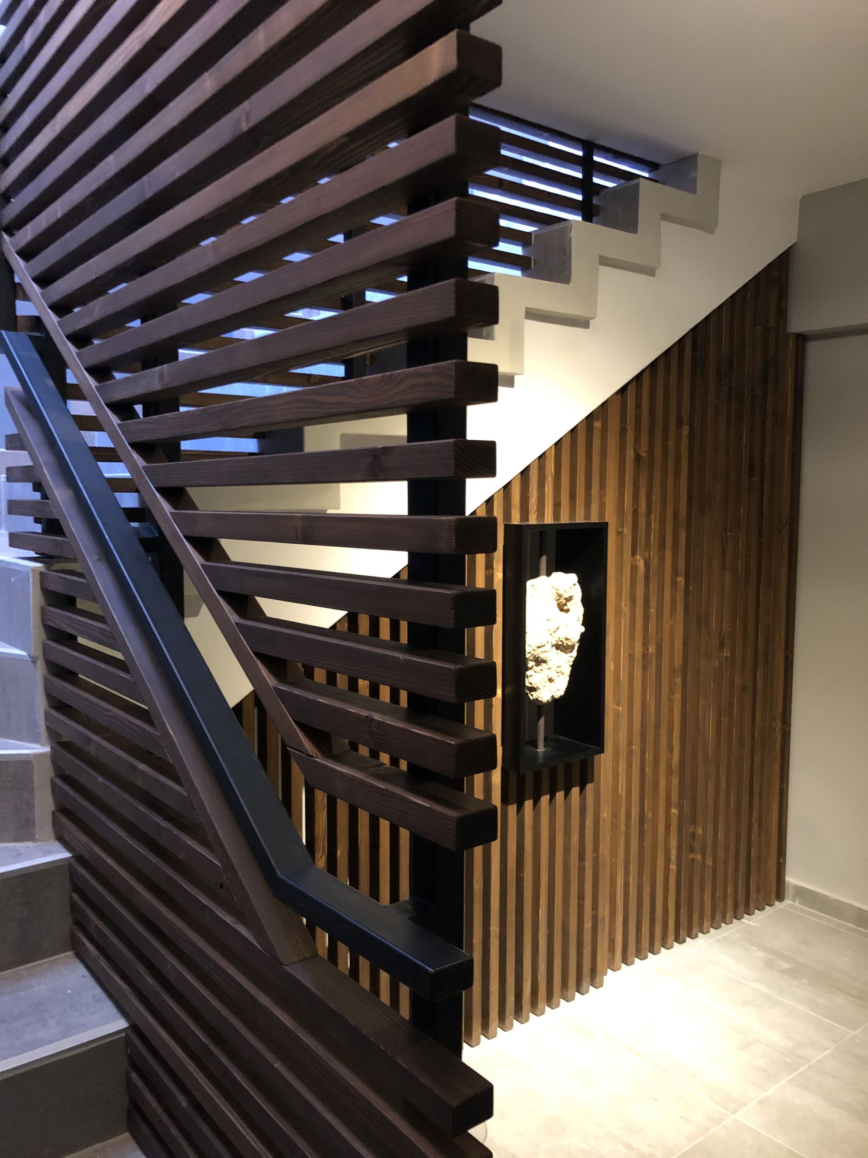 Escadaria moderna com ripas de madeira e corrimão preto.