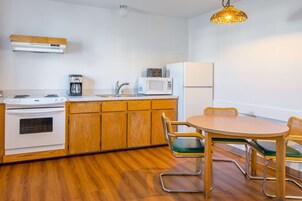 Cozinha compacta com fogão, micro-ondas, máquina de café e geladeira. Há uma mesa de jantar com cadeiras e um lustre.
