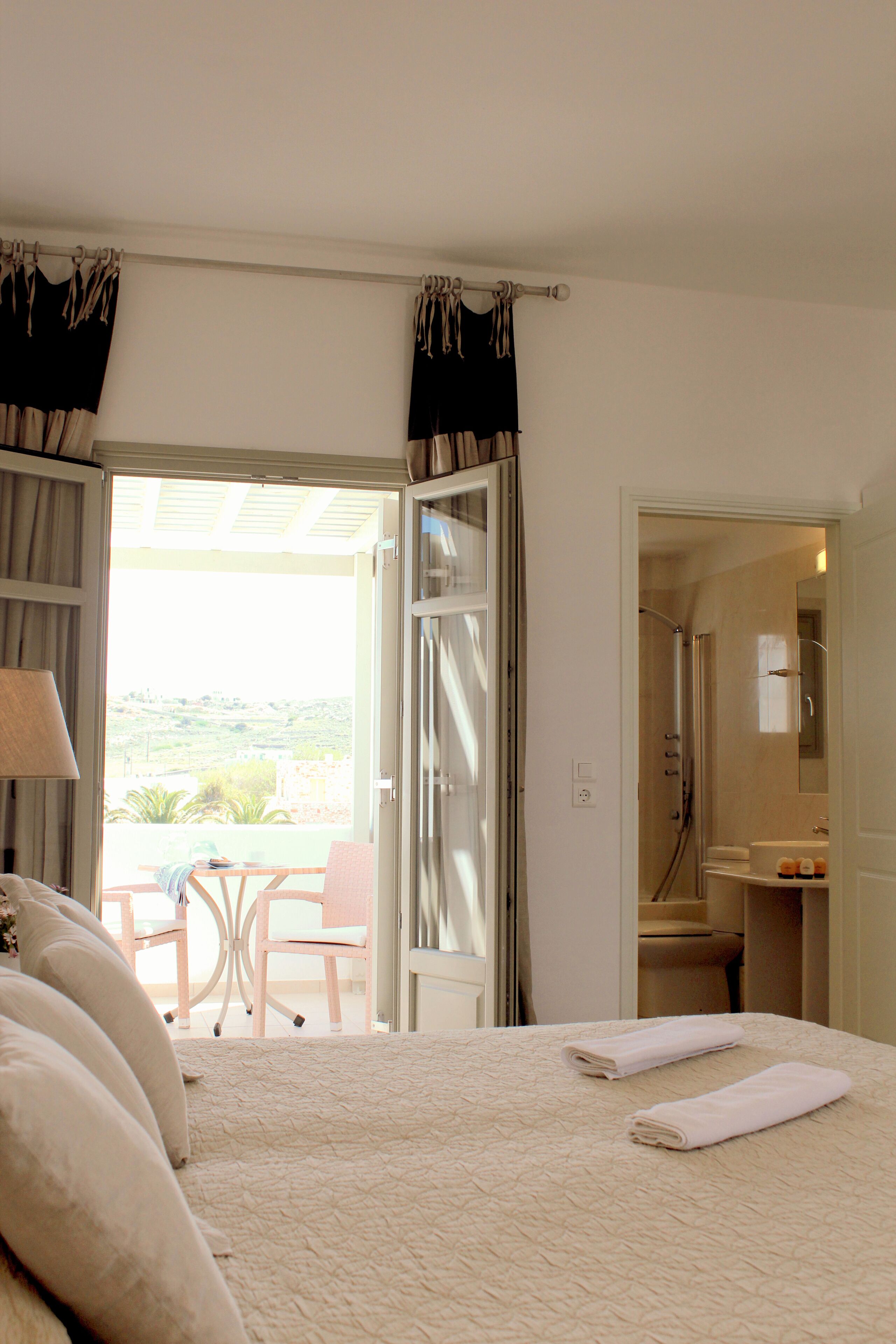 Quarto de hotel com uma cama, uma cadeira, uma mesa e um banheiro visível por uma porta aberta.