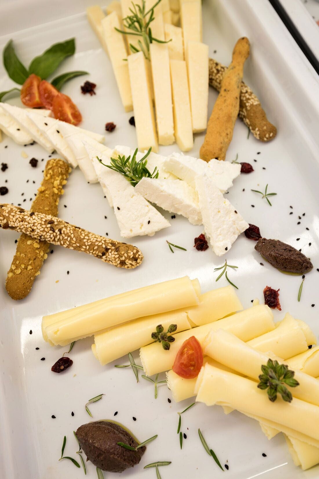 Um prato branco com diversos queijos, biscoitos e ervas.