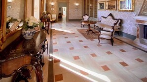 Uma sala ampla com teto ricamente decorado, lustres e móveis clássicos.