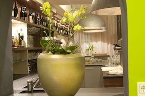 Uma área de bar com uma grande tigela cheia de flores amarelas, prateleiras com garrafas e copos.