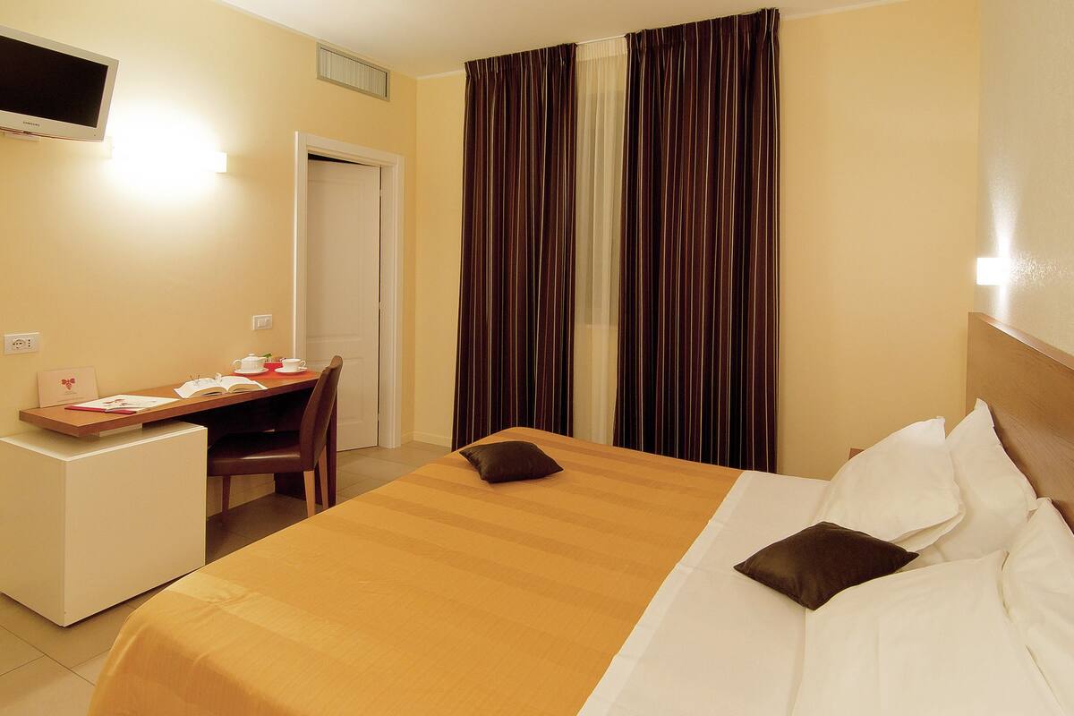 Quarto de hotel com uma cama, uma escrivaninha e uma televisão.