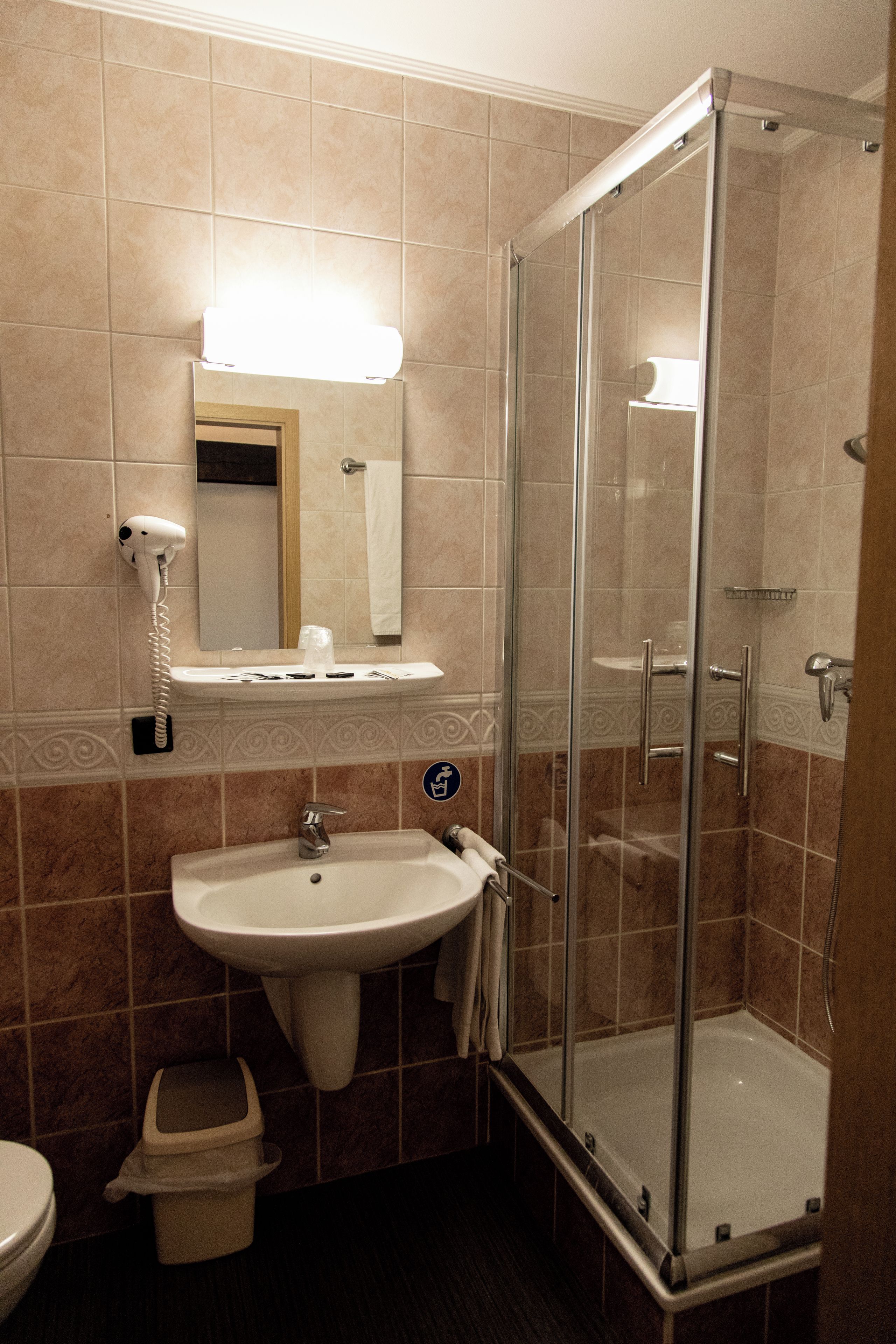 Casa de banho com cabine de duche em vidro, lavatório com toalha e secador de cabelo fixado na parede.