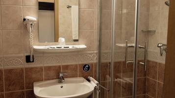 Casa de banho com cabine de duche em vidro, lavatório com toalha e secador de cabelo fixado na parede.