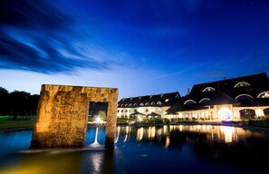 Estrutura de pedra com a inscrição "HOTEL REMES", um espelho d'água refletor e um edifício com várias janelas em arco e um telhado com janelas salientes.