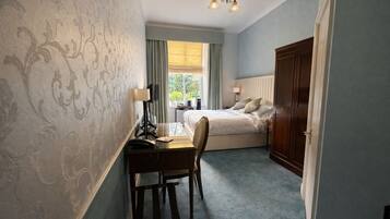 Quarto de hotel com cama, escrivaninha com cadeira, guarda-roupa e janela com cortinas.