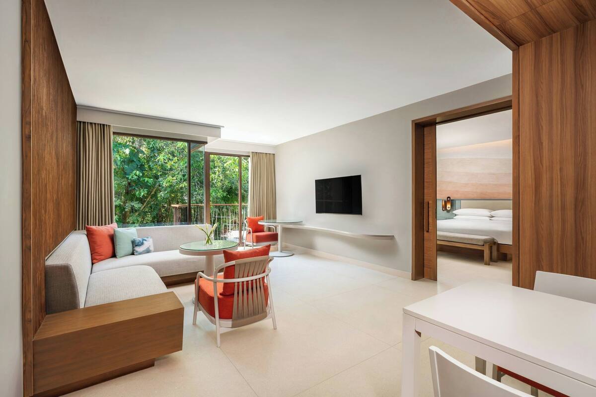 Quarto de hotel moderno com sofá, mesa de jantar e TV fixada na parede.