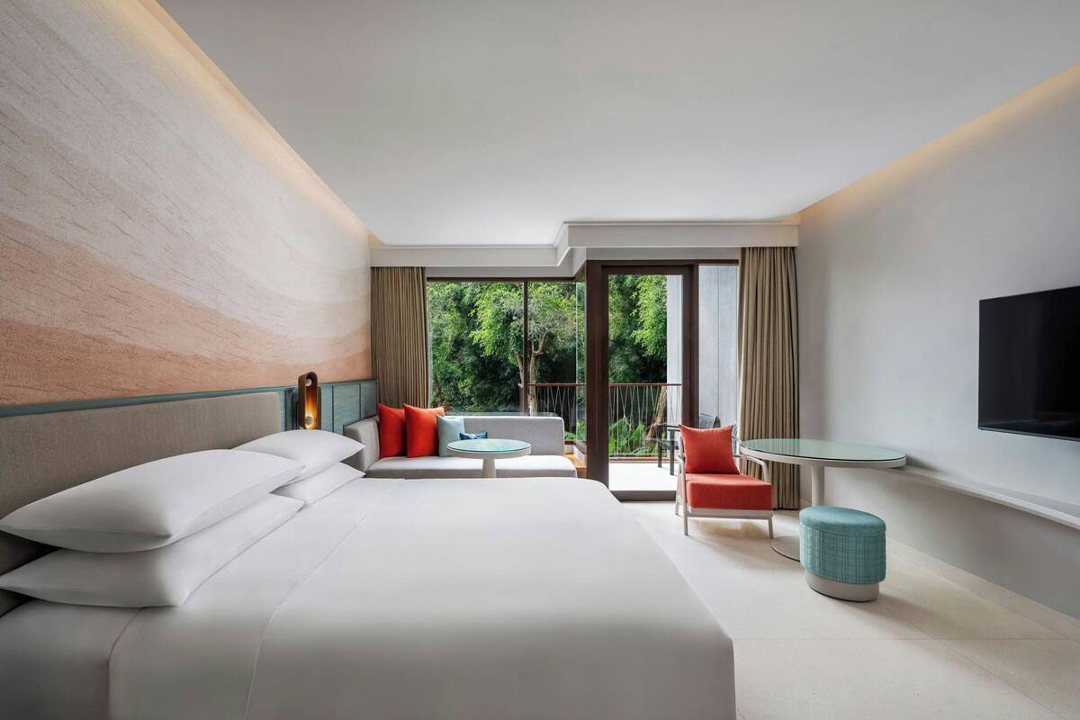 Quarto de hotel moderno com uma cama grande, uma mesa pequena, um sofá e uma televisão.