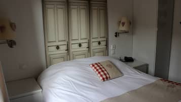 Cama bem arrumada com travesseiro xadrez, luminária de cabeceira e telefone em uma mesinha de cabeceira.