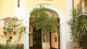 Entrada de um edifício com um arco, plantas em vasos e uma placa com o número do prédio.