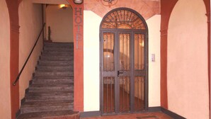 Escadaria que leva à entrada de um hotel, com um portão de metal decorativo e uma placa acima.