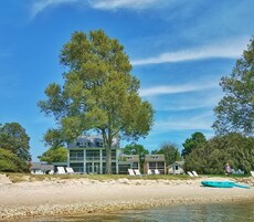 Um imóvel à beira-mar com uma grande árvore, vários edifícios e cadeiras de praia.