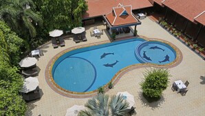 Uma piscina com desenhos de golfinhos, rodeada por espreguiçadeiras e guarda-sóis, com um edifício ao fundo.