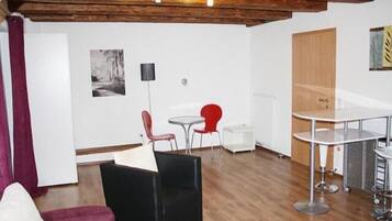 Quarto moderno com teto de madeira, sofá preto, cadeira vermelha, mesa branca e um pequeno armário branco.