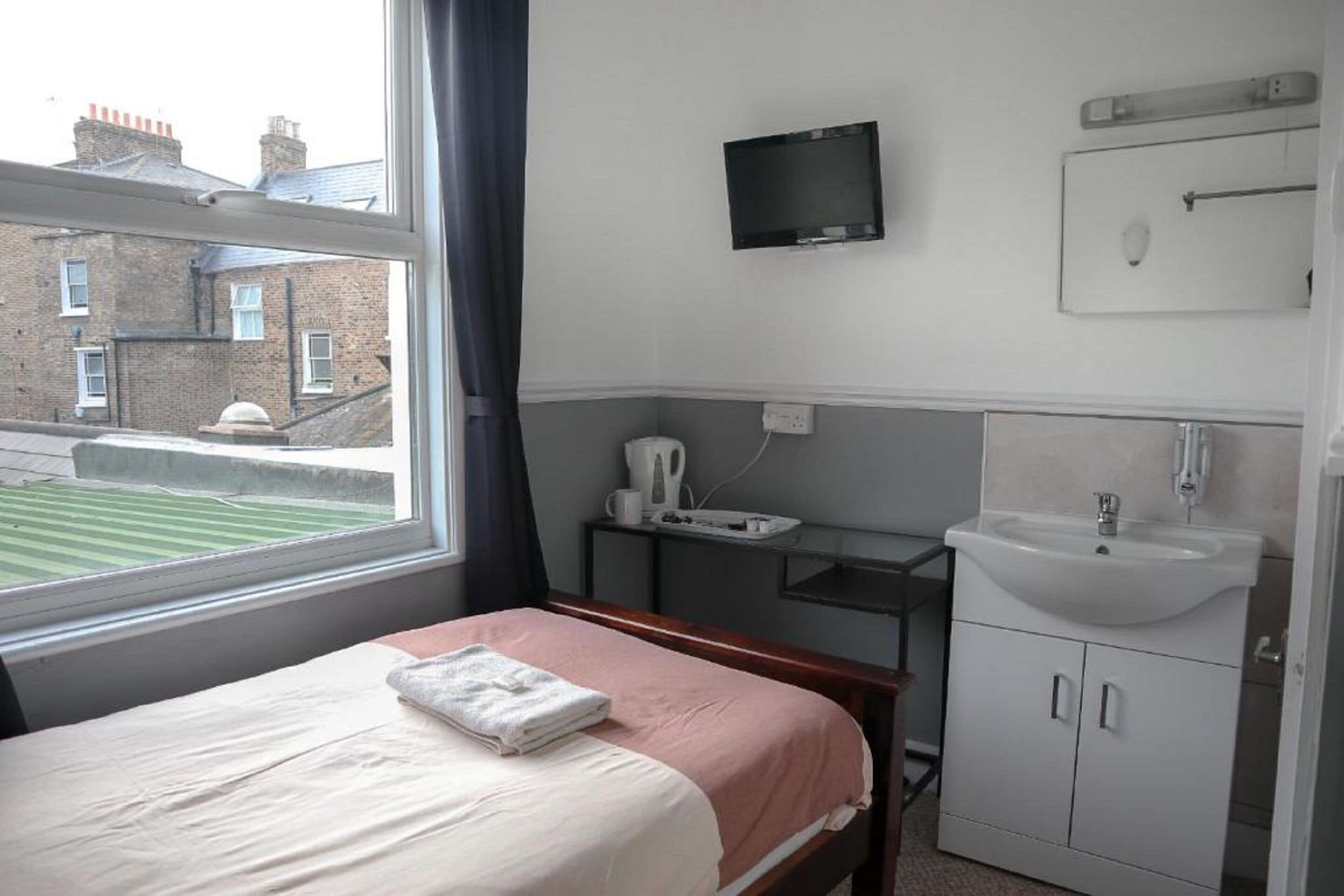 Quarto com cama, TV, pia e janela com vista para edifícios.