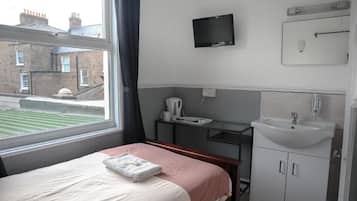 Quarto com cama, TV, pia e janela com vista para edifícios.