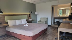 Quarto de hotel com cama, mesa de cabeceira, luminária, cadeira, escrivaninha e vista para o exterior.