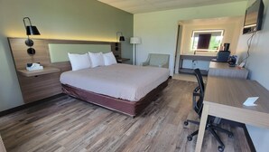 Quarto de hotel com cama, mesas de cabeceira, escrivaninha, cadeira, luminária, televisão e janela.
