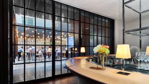 Uma área de bar moderna com balcão curvo, grandes janelas e vista para uma sala de jantar animada.