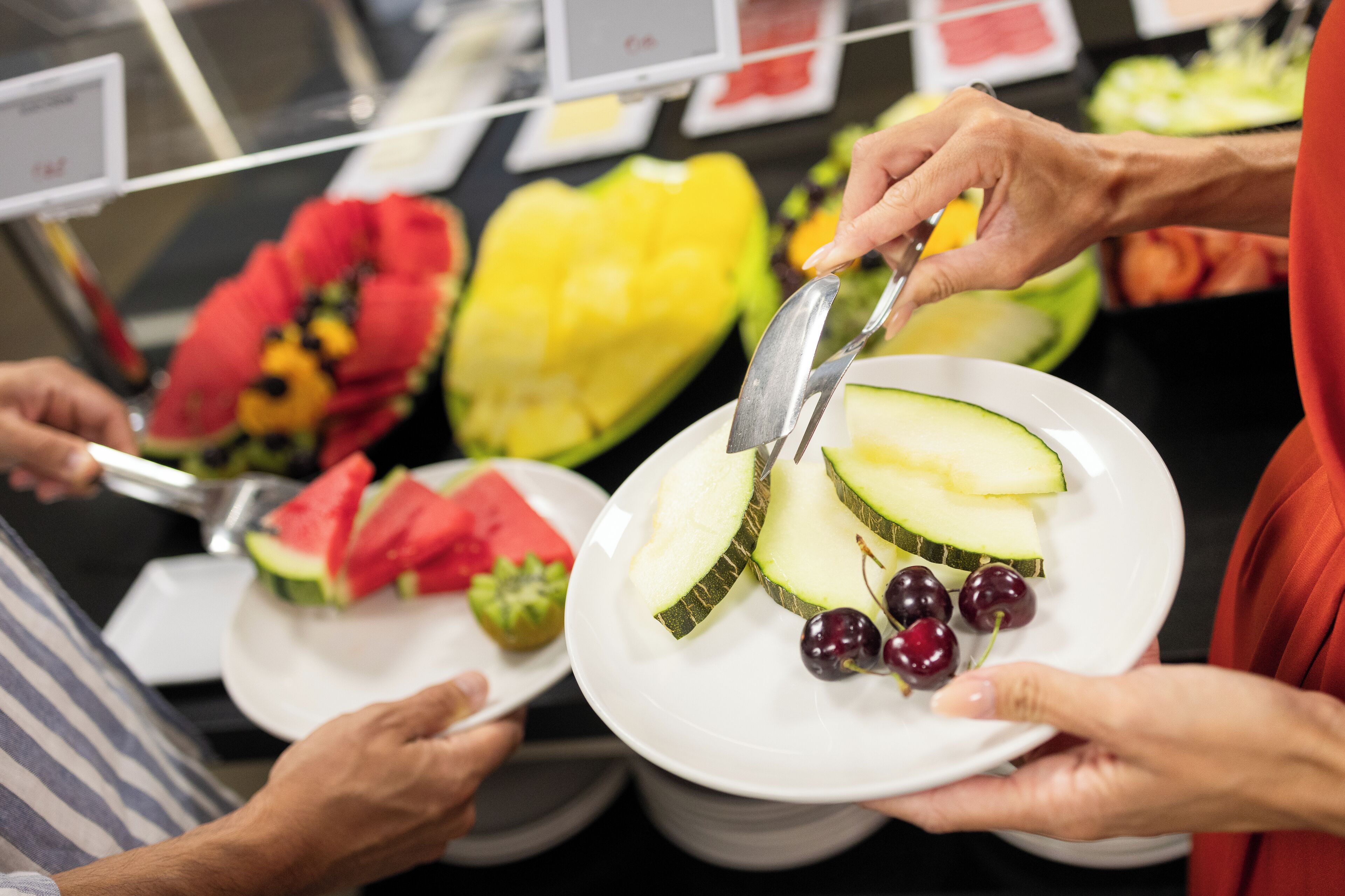 Uma pessoa se servindo de frutas em um buffet.