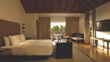 Quarto de hotel moderno com uma cama grande, escrivaninha, cadeira, televisão e varanda com vista para palmeiras.