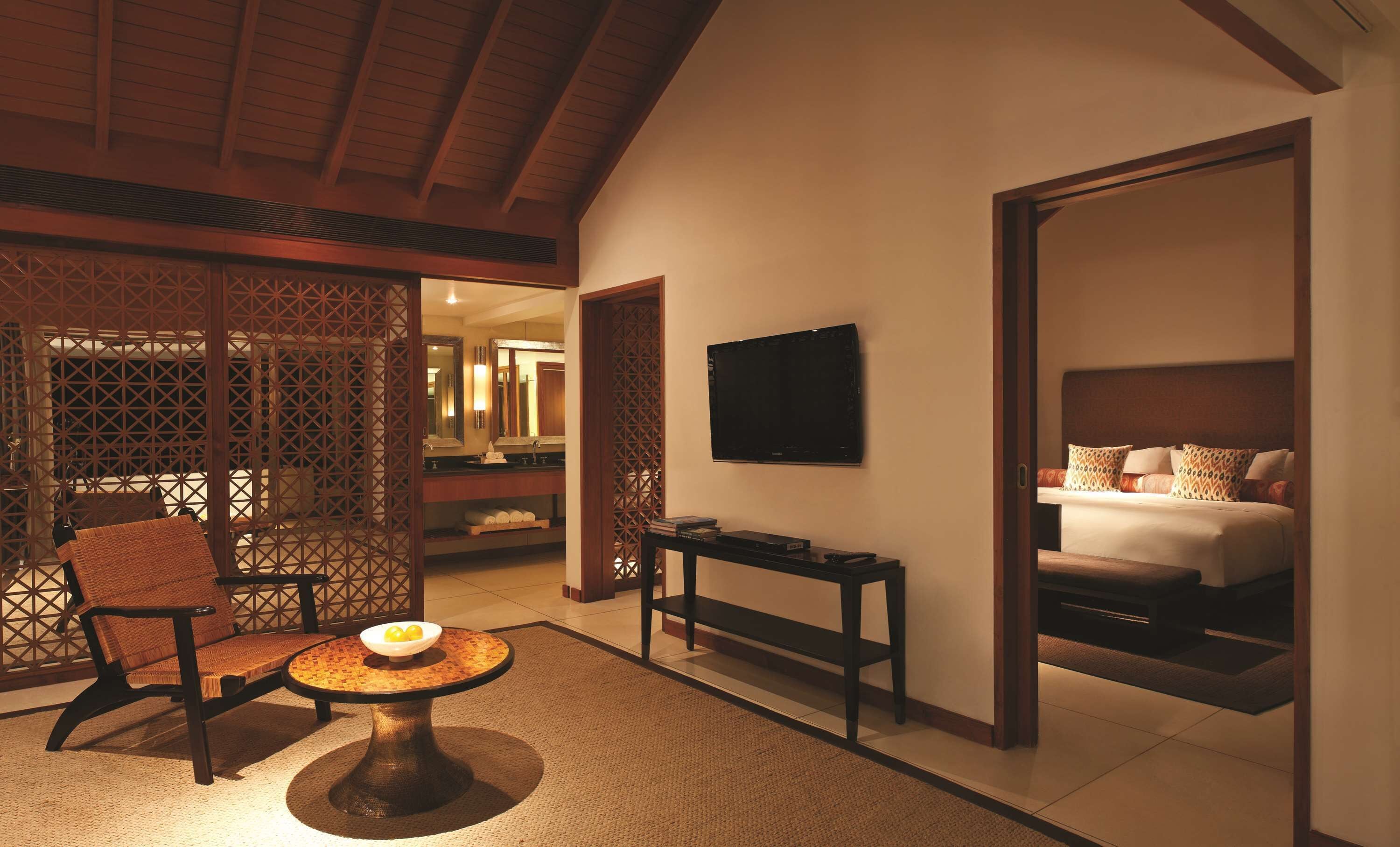 Quarto de hotel com cama, televisão, poltrona, mesa e um ecrã decorativo.
