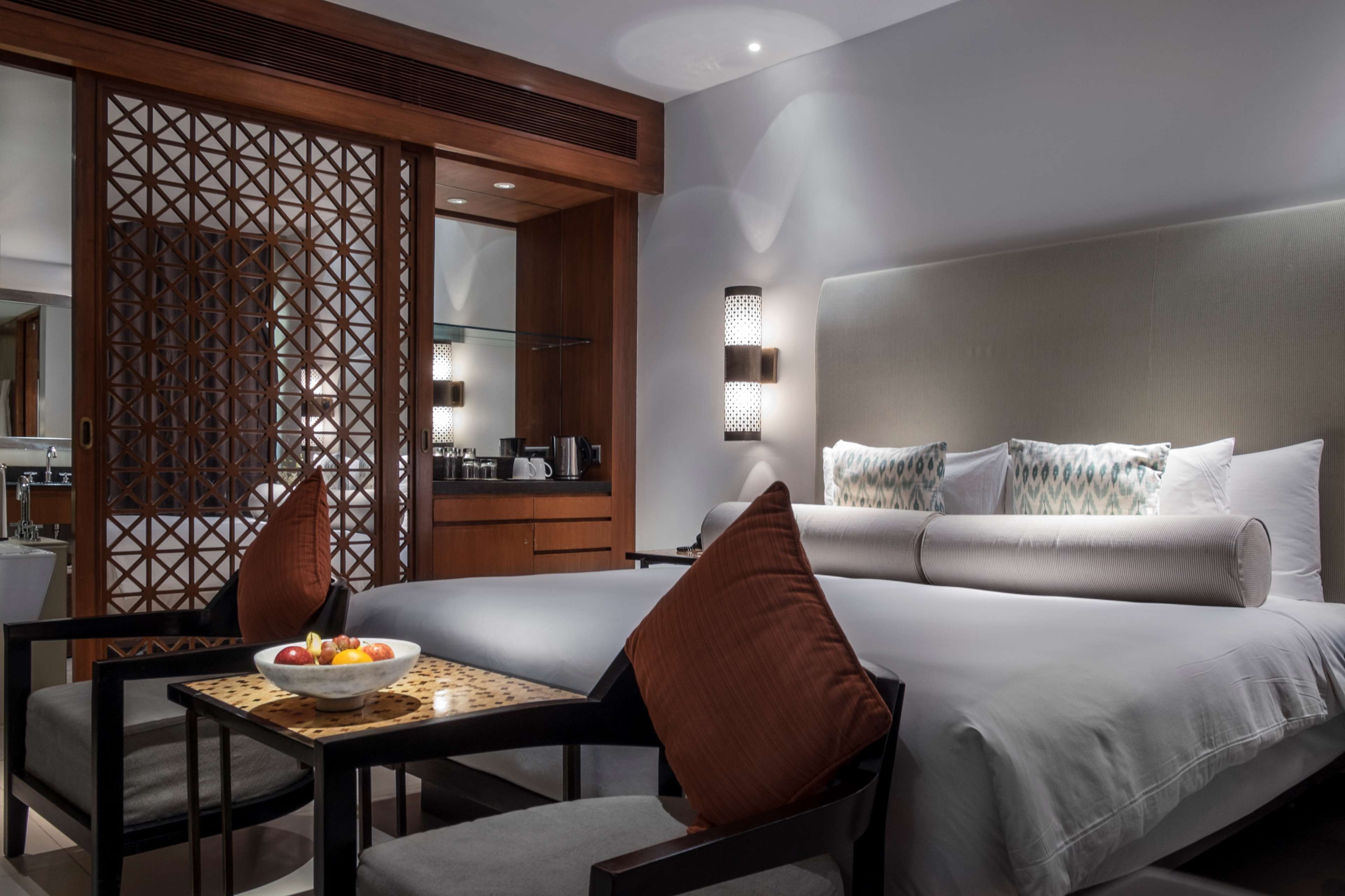 Quarto de hotel moderno com uma cama grande, uma mesa de jantar com uma tigela de frutas e uma área de estar separada.