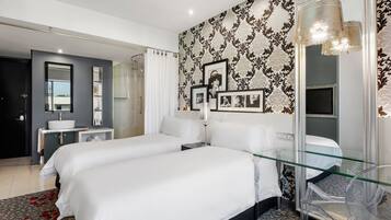 Quarto de hotel moderno com duas camas, uma escrivaninha de vidro e um espelho grande.