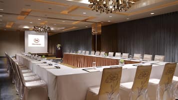 Uma sala de conferências com uma mesa comprida, cadeiras e uma tela exibindo o logotipo Sheraton.
