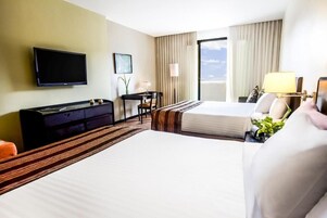 Quarto de hotel com duas camas, televisão, escrivaninha e vista do céu.