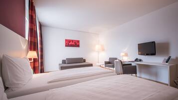 Quarto de hotel com duas camas, uma escrivaninha, uma cadeira, uma televisão e uma obra de arte vermelha na parede.