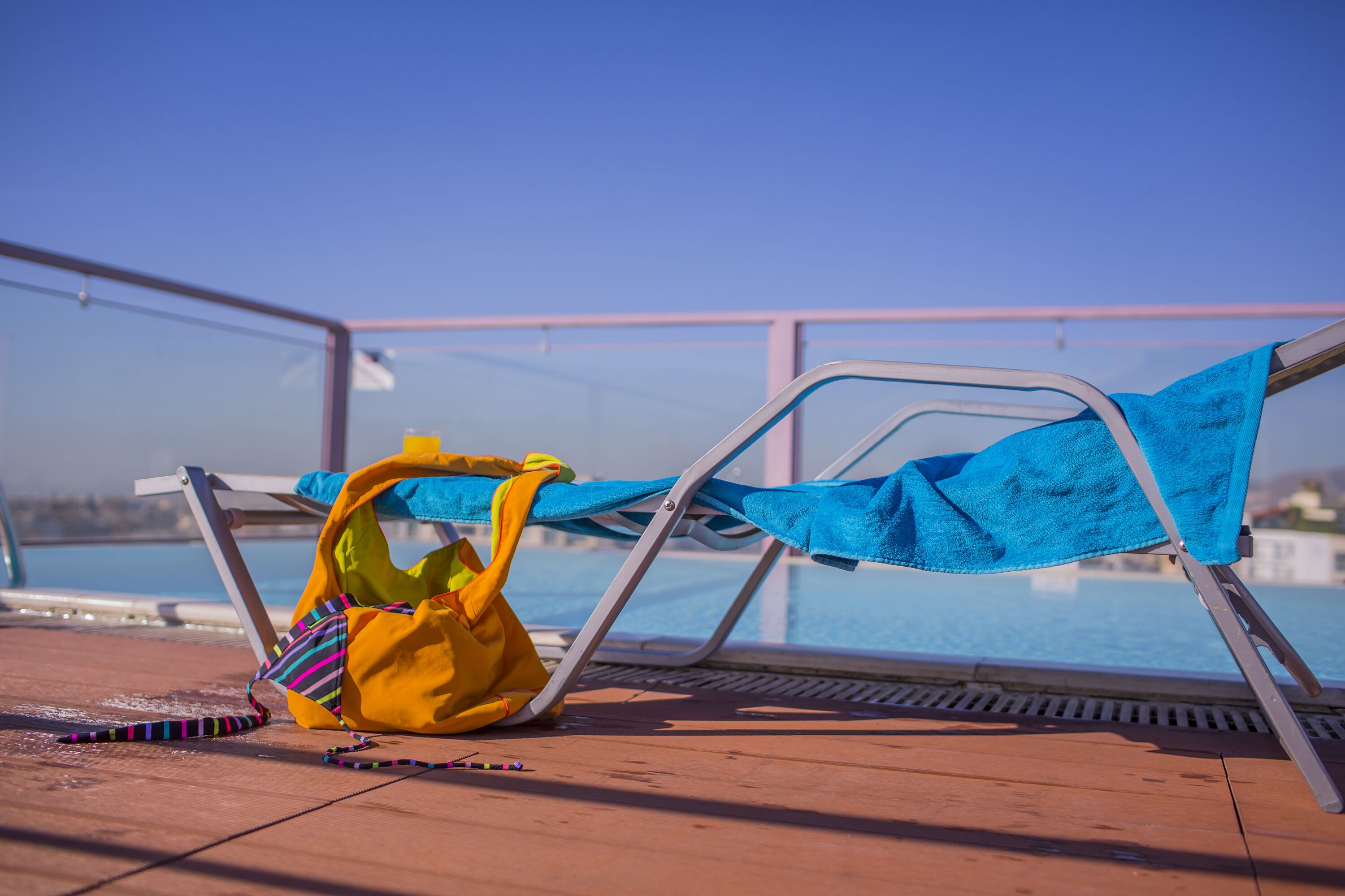 Uma área na beira da piscina com uma espreguiçadeira e uma bolsa amarela no deck.