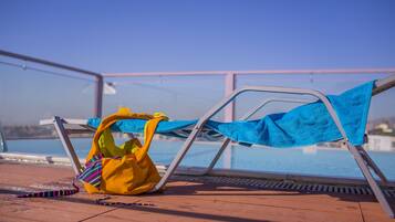 Uma área na beira da piscina com uma espreguiçadeira e uma bolsa amarela no deck.
