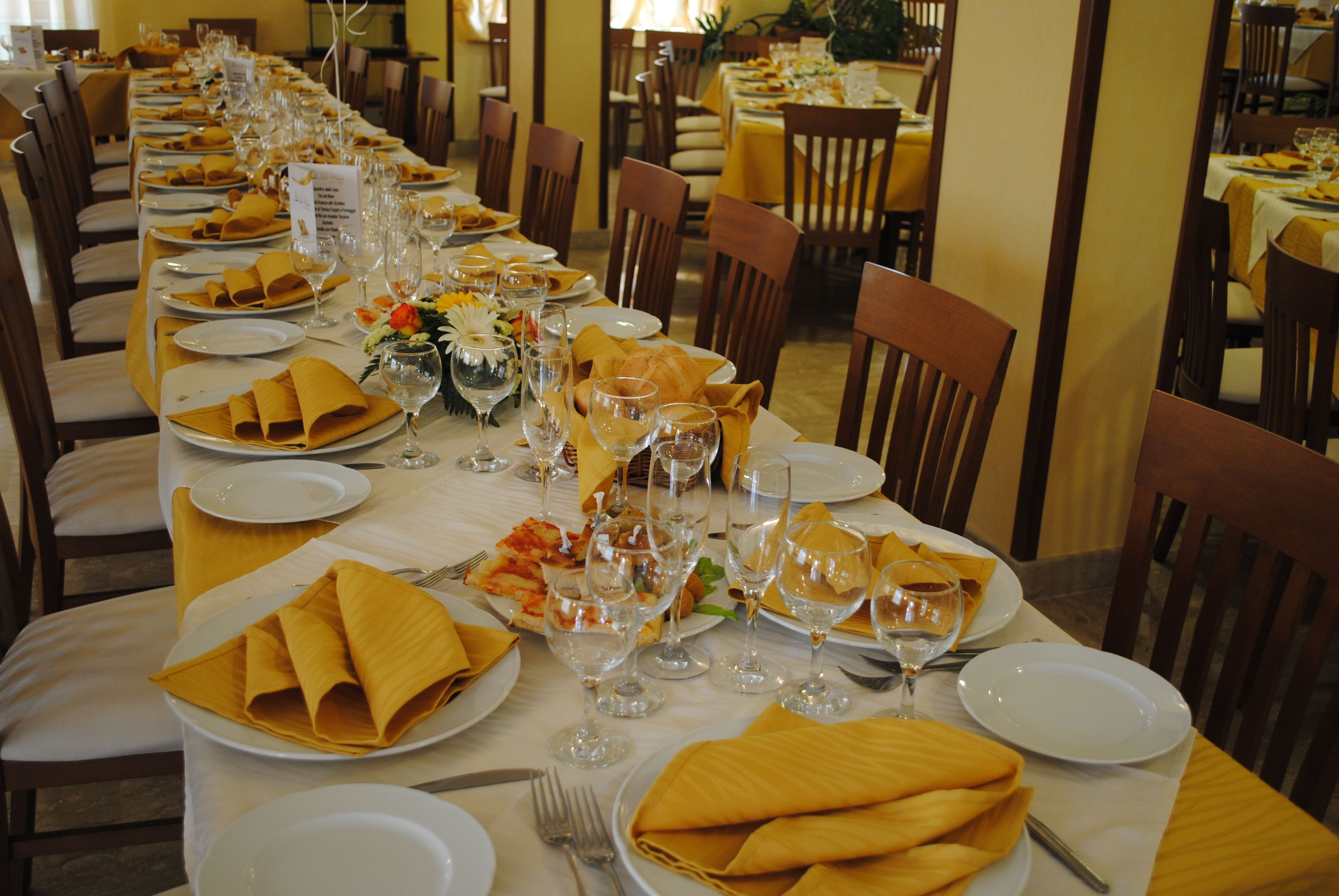 Uma longa mesa de jantar posta com várias cadeiras, pratos, talheres e copos de vinho.